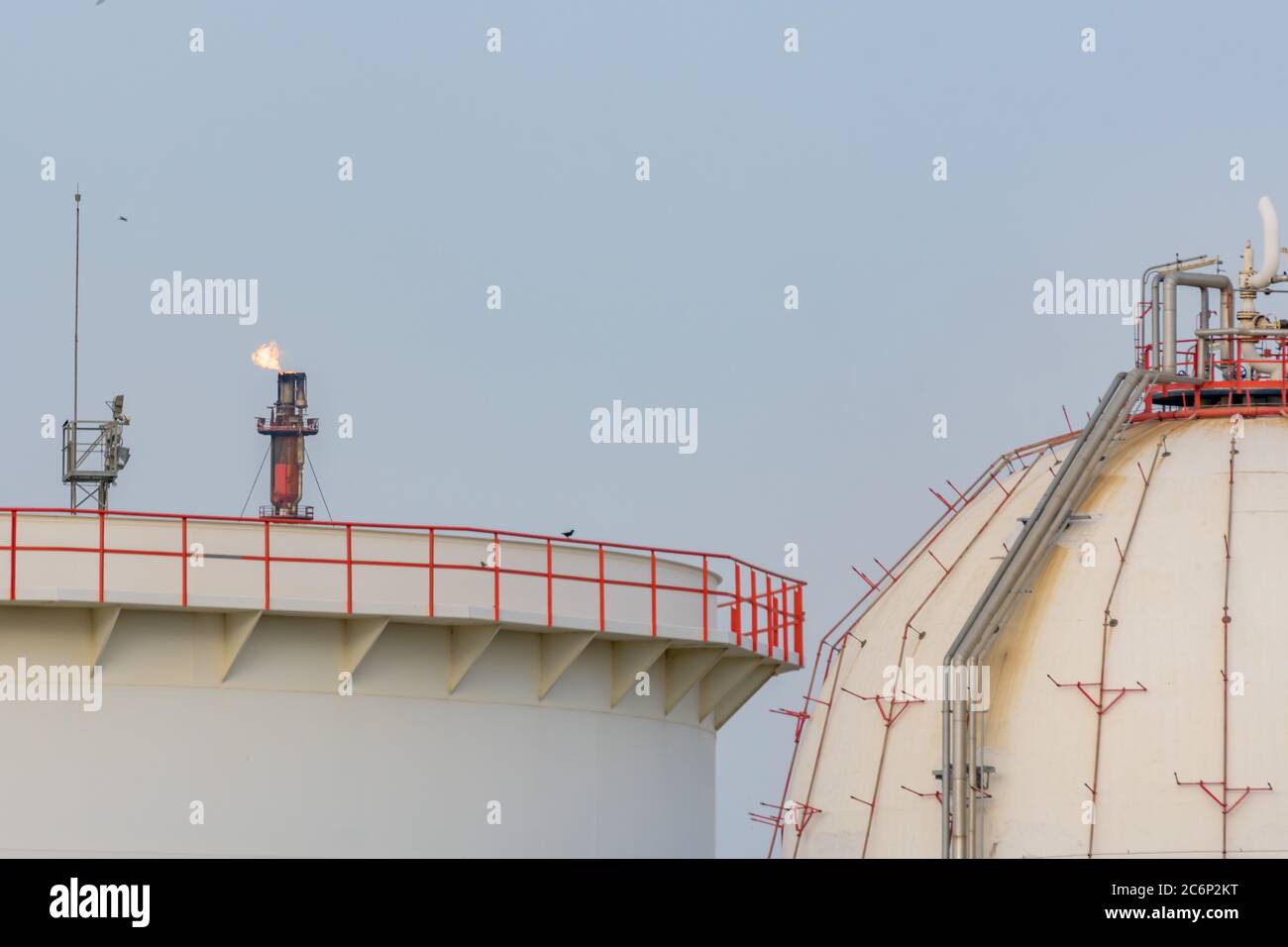 Torch of an oil refinery protruding above fuel tanks Stock Photo - Alamy