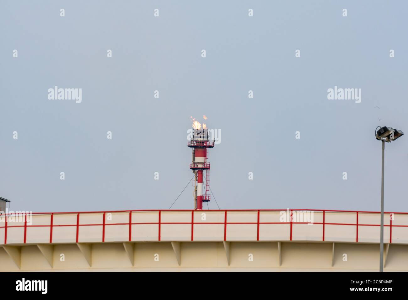 Torch of an oil refinery protruding above fuel tanks Stock Photo - Alamy