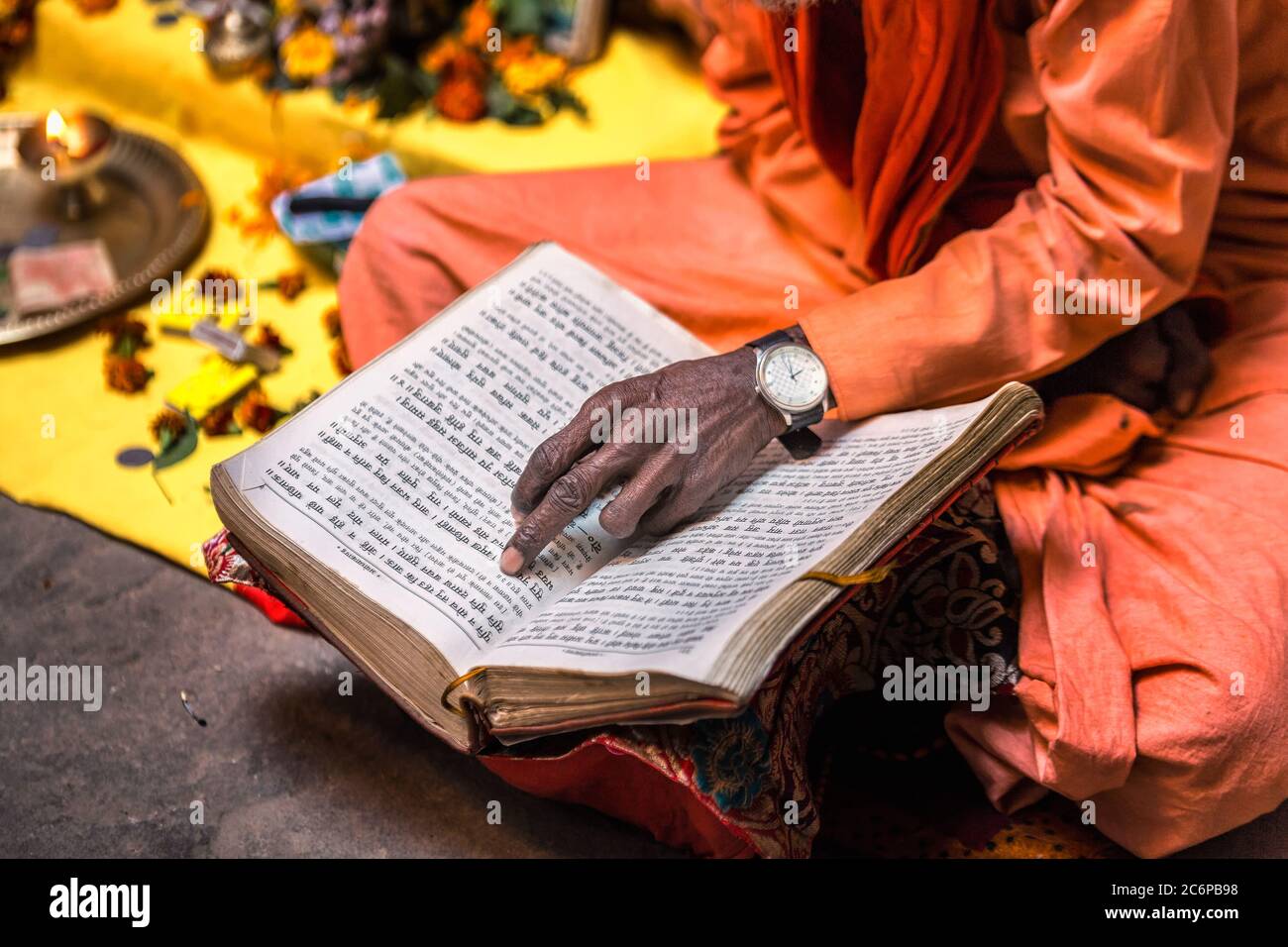 Old sadhu hand wearing hand watch pointing at line of holy book ...