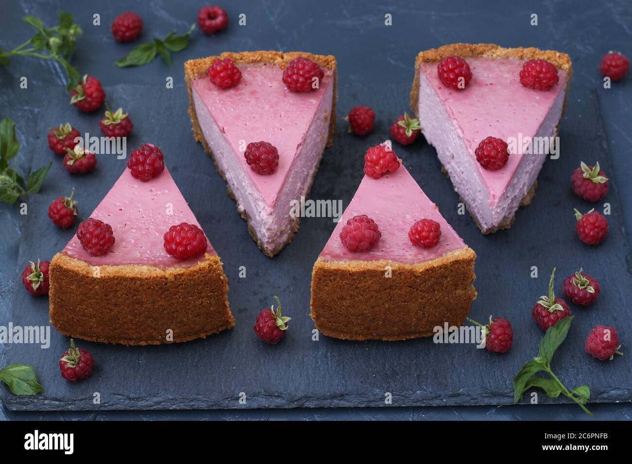 Chopped homemade raspberry cheesecake in portions on a plate on dark ...