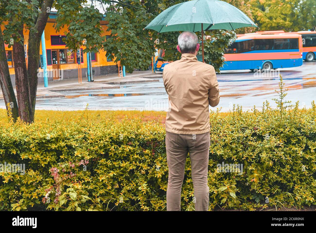 A man standing at the bus station with an umbrella waiting for a bus ...