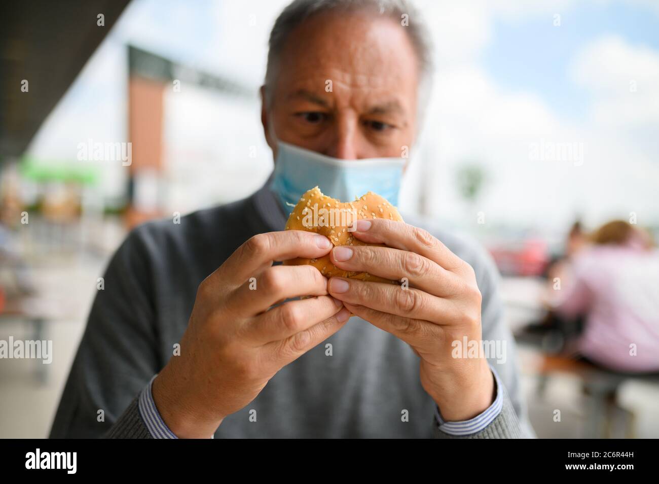 Mature man trying to eat a hamburger wearing a mask, funny coronavirus ...