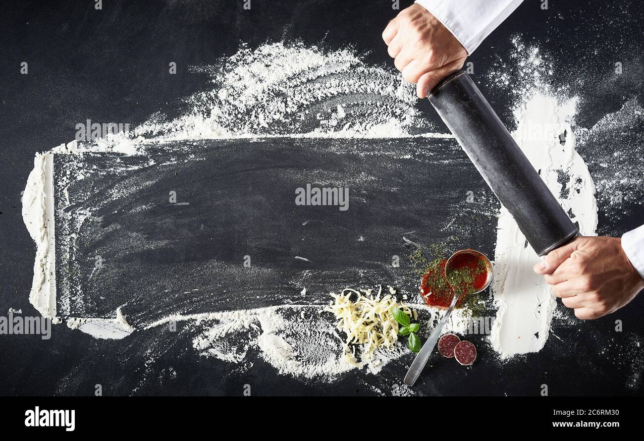 Chef rolling out flour with Italian cooking ingredients for pizzas ...