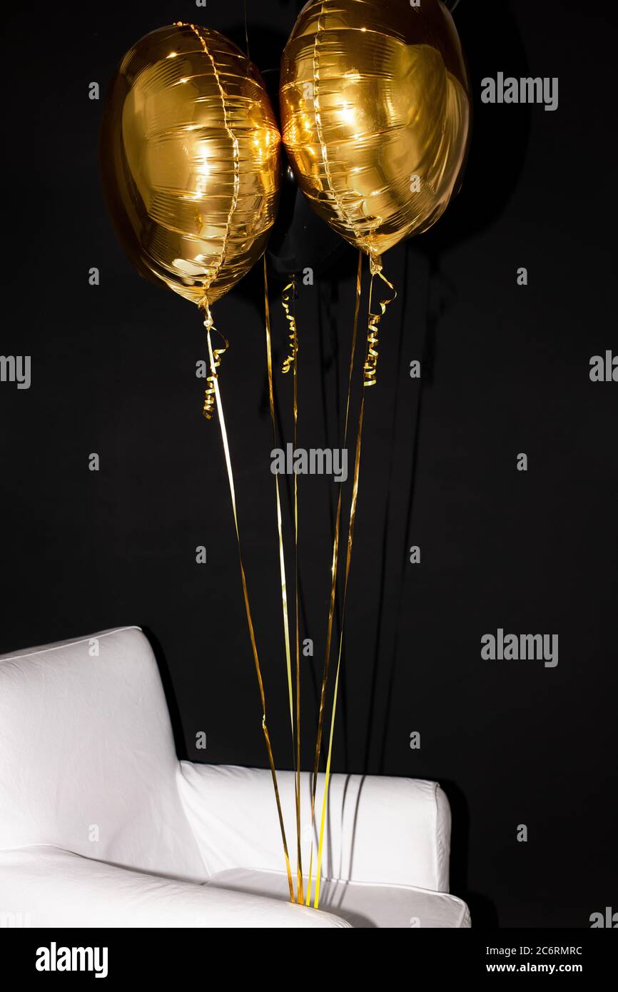 Bunch of inflated golden color balloons bound to white leather armchair ...