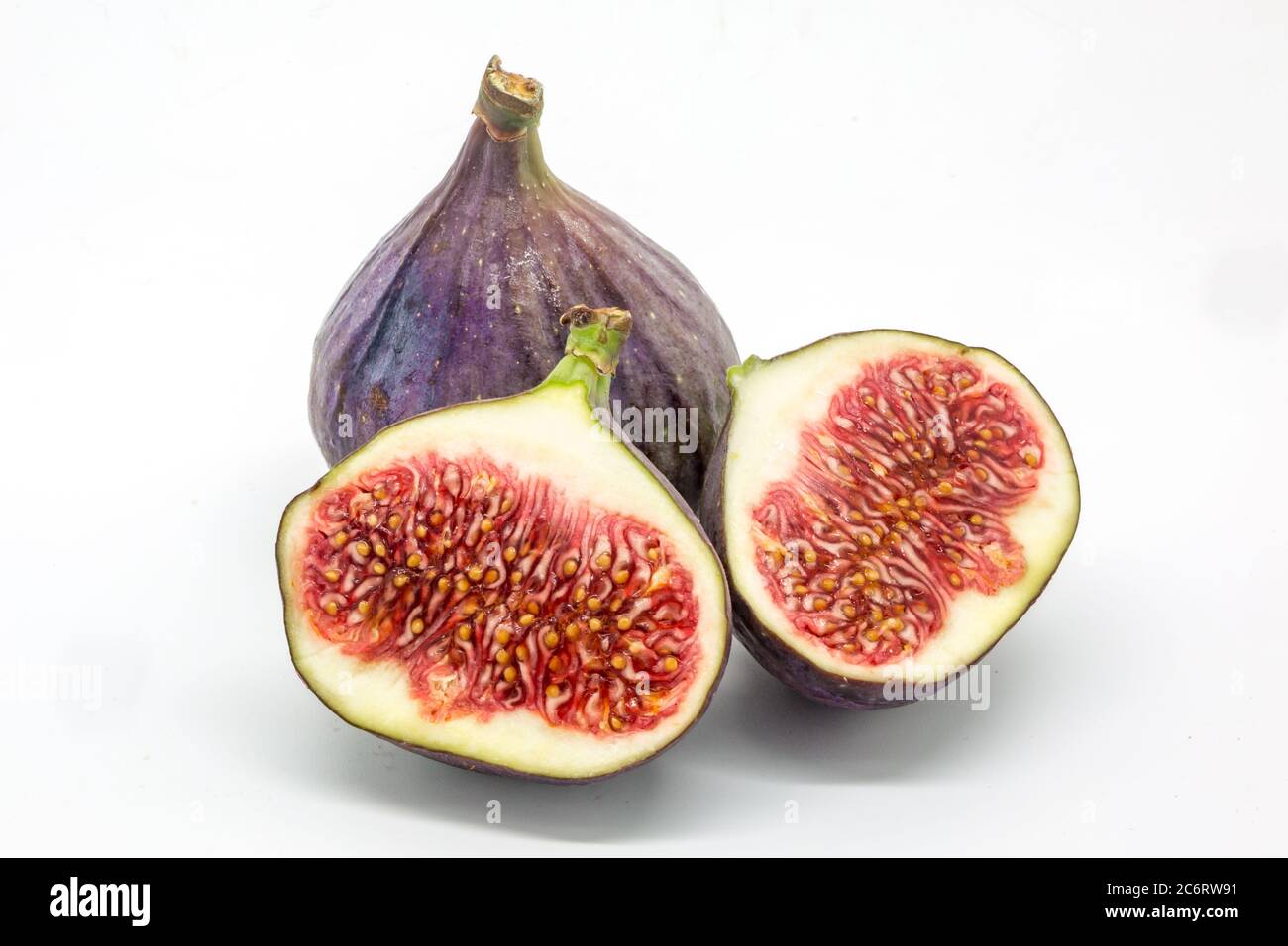Two figs, one cut in half to show the seeds, against a white background ...