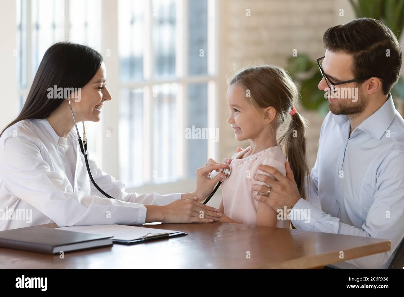 Smiling female doctor using stethoscope, listening to little girl ...