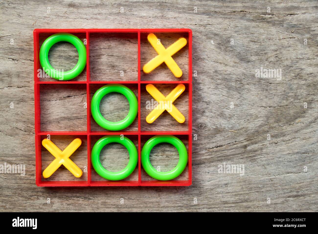 Tic-tac-toe board game with green O and yellow X in red frame on wood ...