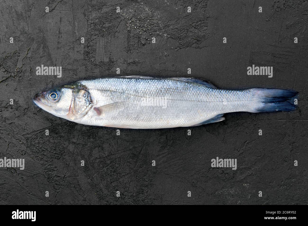 Raw seabass fish on black stone table Stock Photo - Alamy