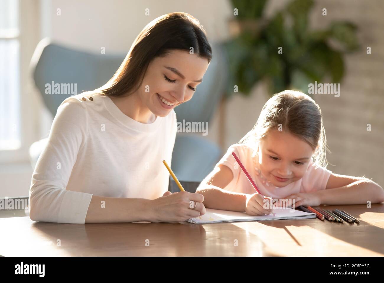 Smiling woman drawing colorful pencils with adorable little daughter ...