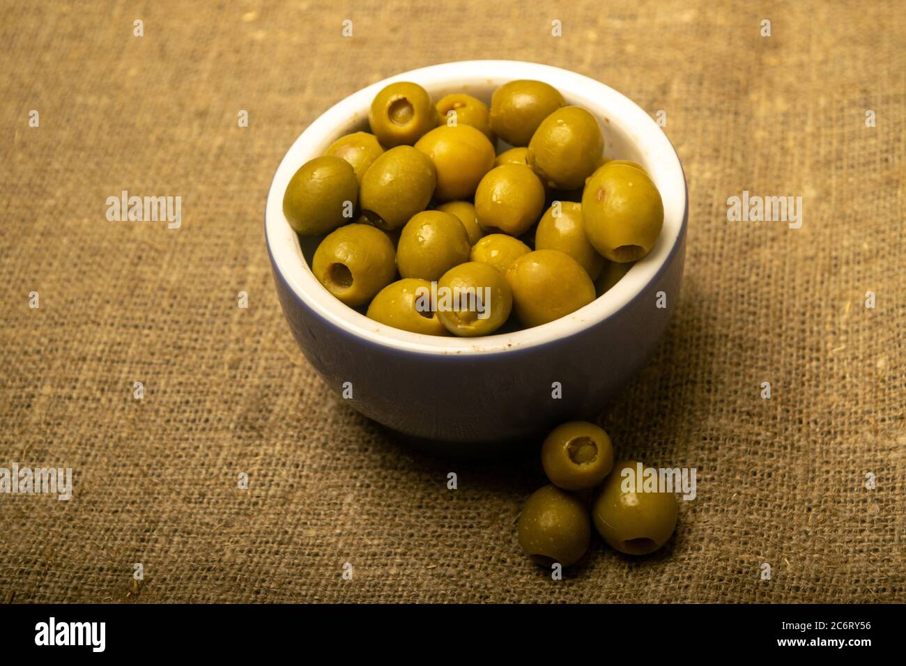 Green olives in a ceramic bowl on a background of coarse-textured ...