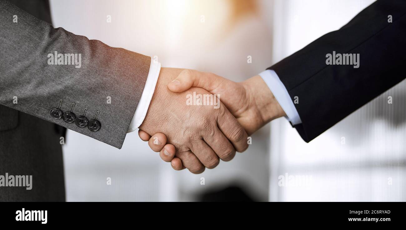 Business people standing and shaking hands in sunny office, close-up ...