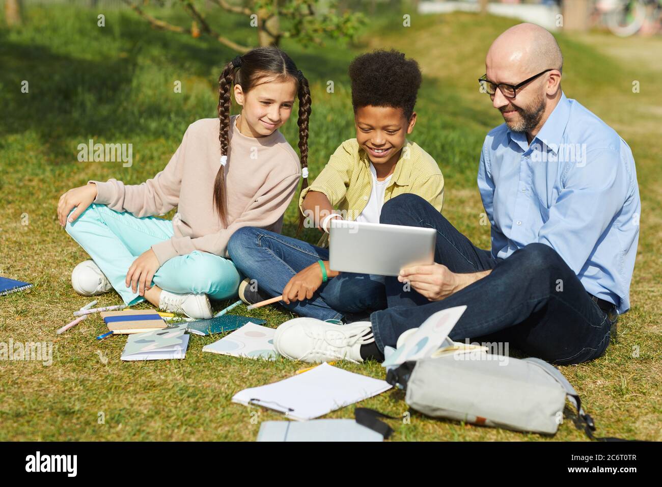 Full length portrait of smiling male teacher talking to children while ...