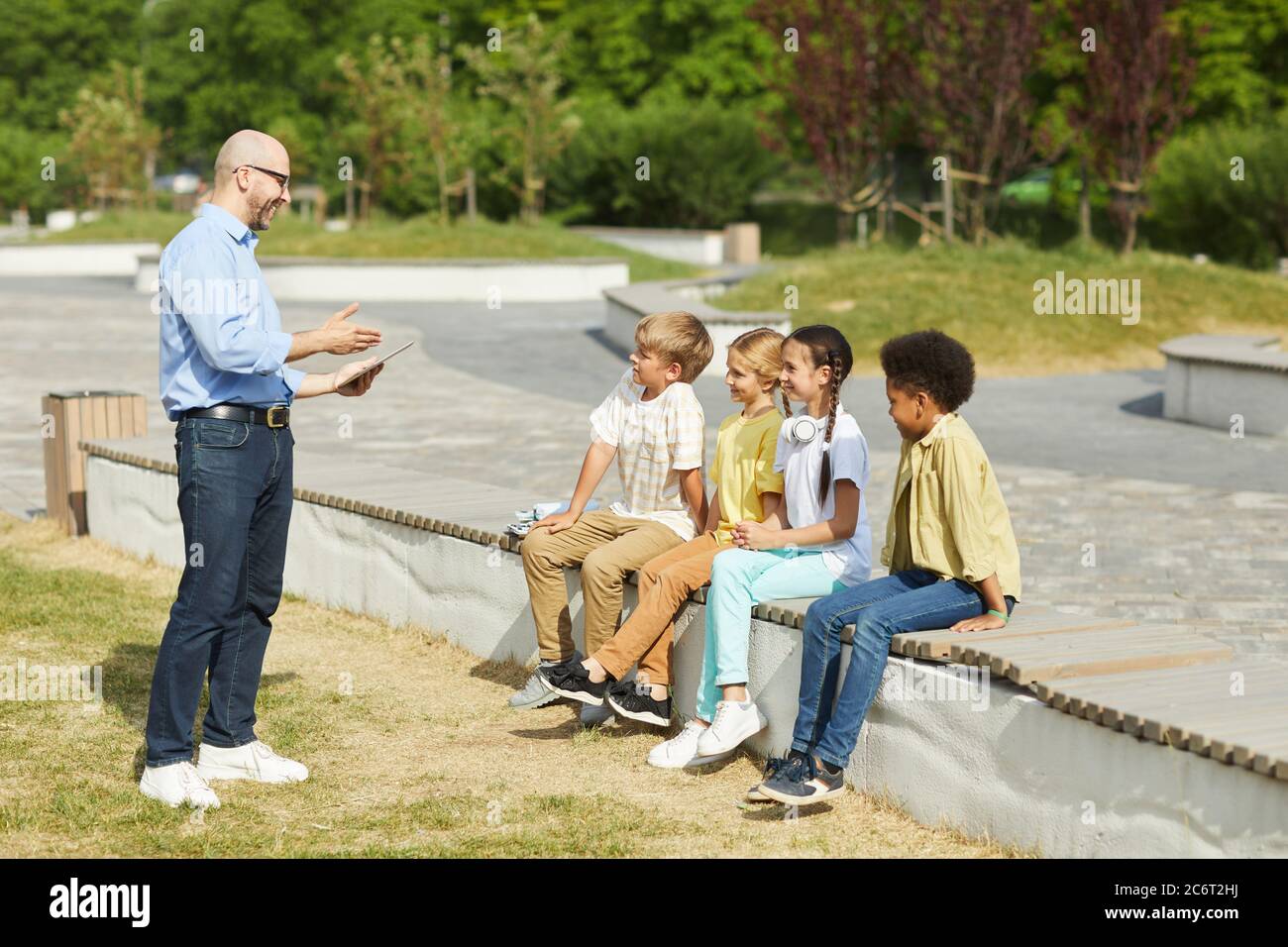 Full length portrait of smiling male teacher talking to group of ...
