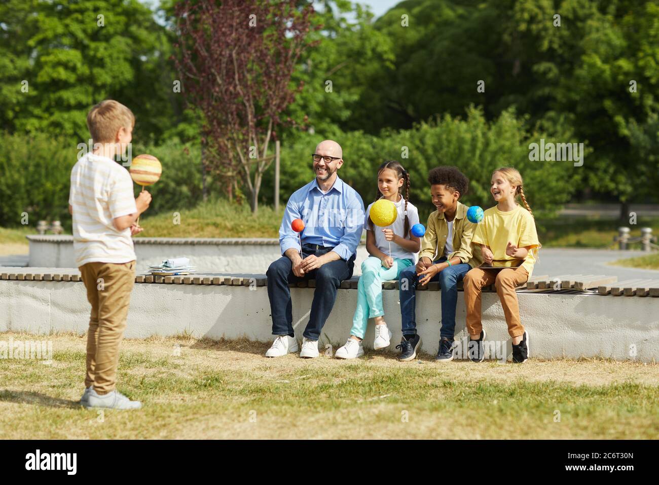 Full length portrait of smiling male teacher listening to boy giving ...