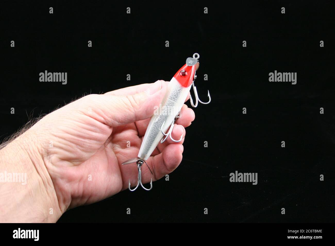 Black background of old man's hand holding fishing lure with hooks ...