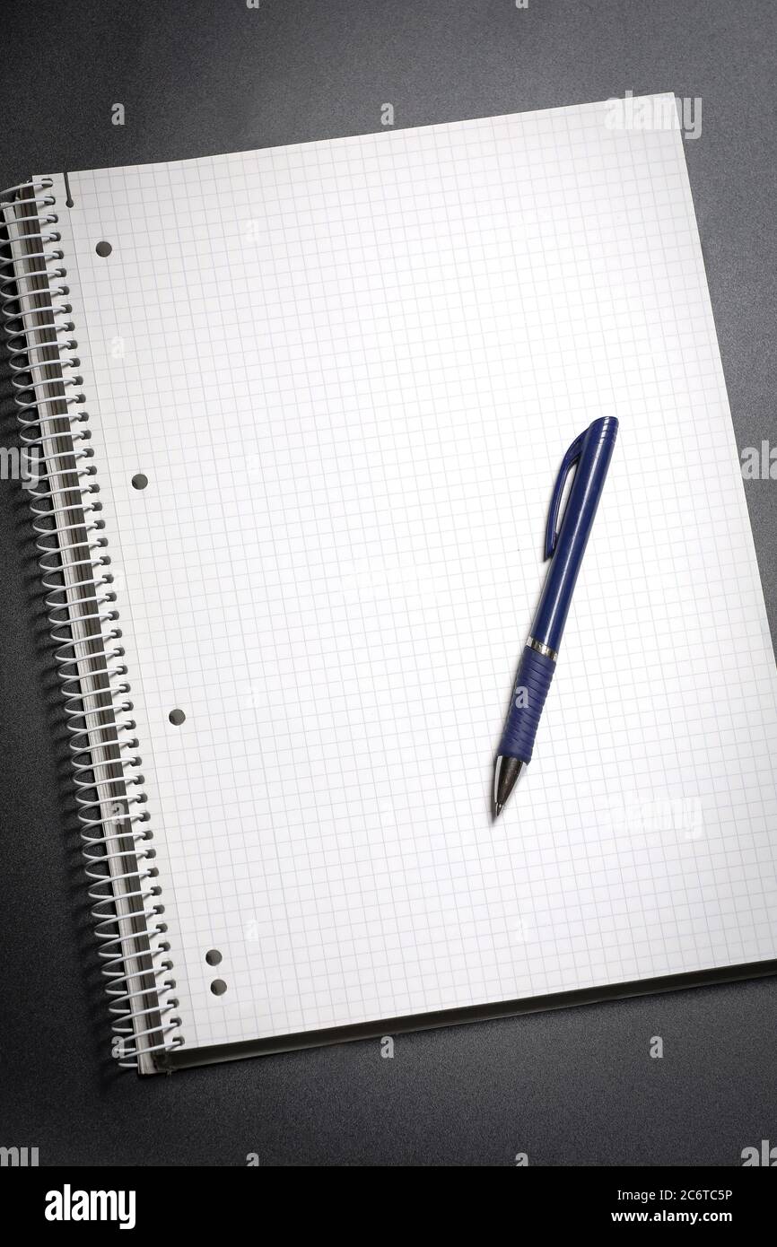 Flat lay view of a white notebook and blue pen on a black table. Copy ...