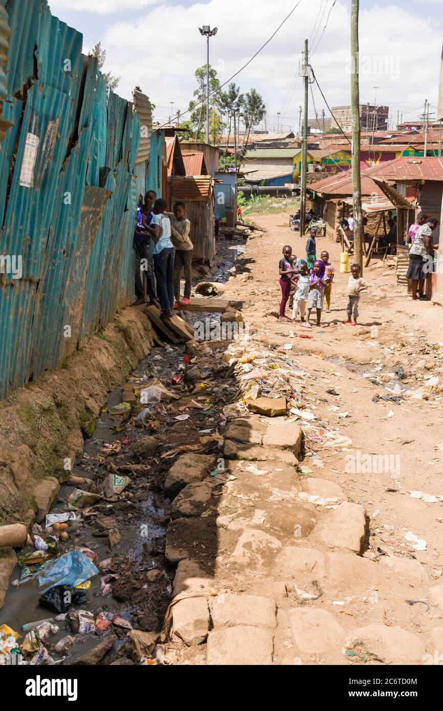 Children playing on a dirt alley way with open sewer filled with ...