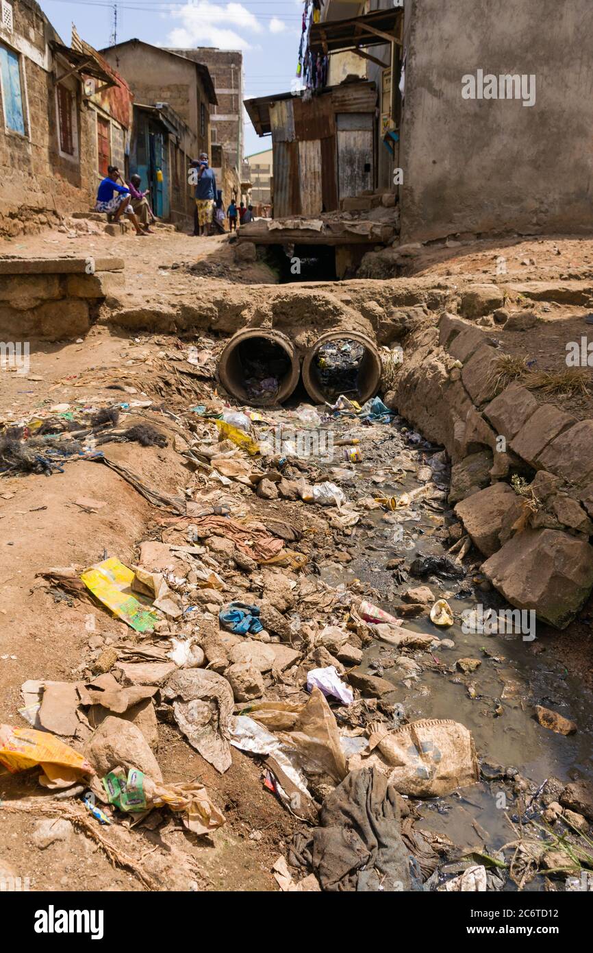 An open sewer filled with rubbish by the side of a dirt alley with ...