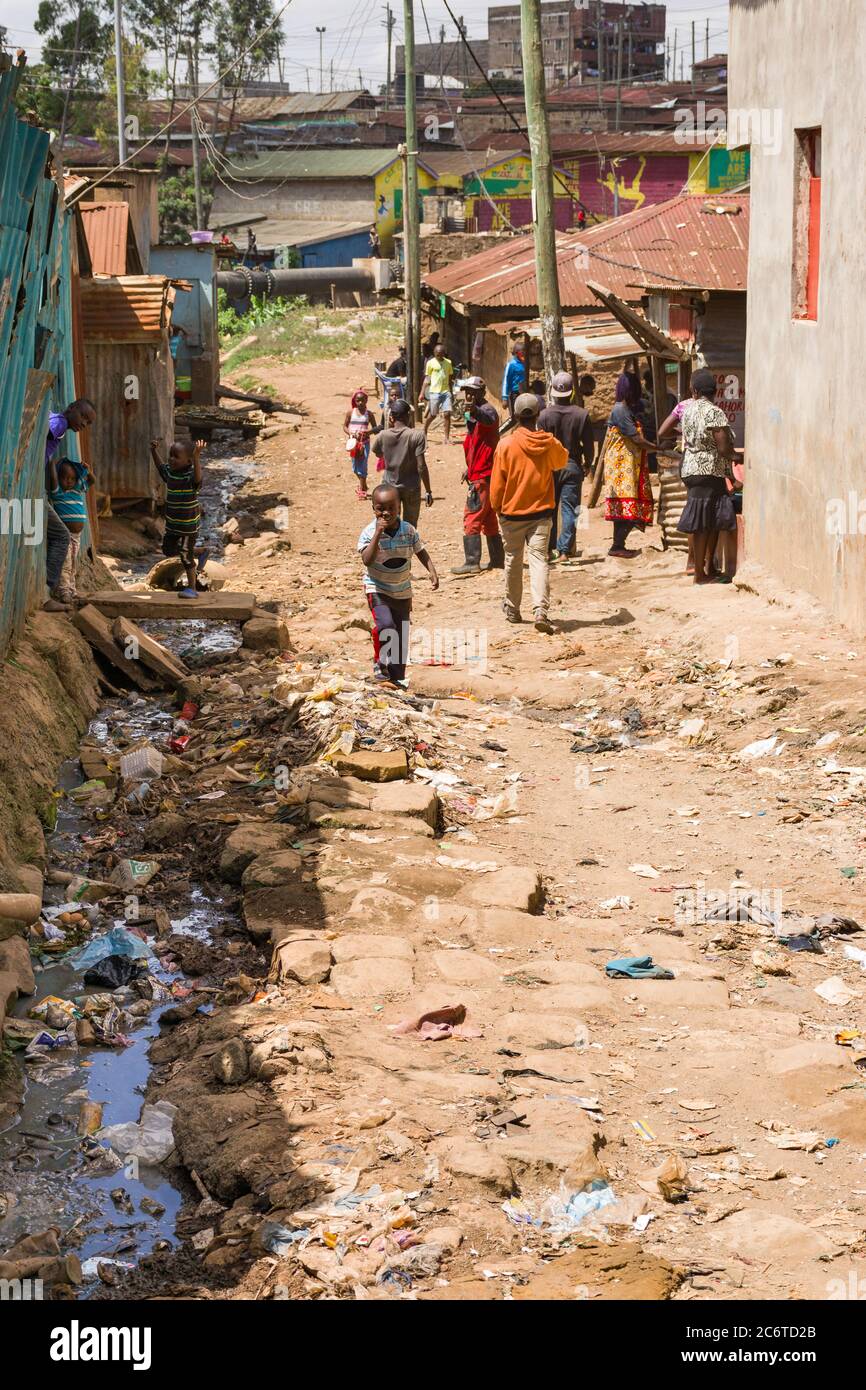 An open sewer filled with rubbish by the side of a dirt alley with ...