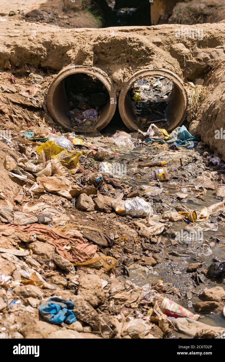 An open sewer filled with rubbish by the side of a dirt alley ...