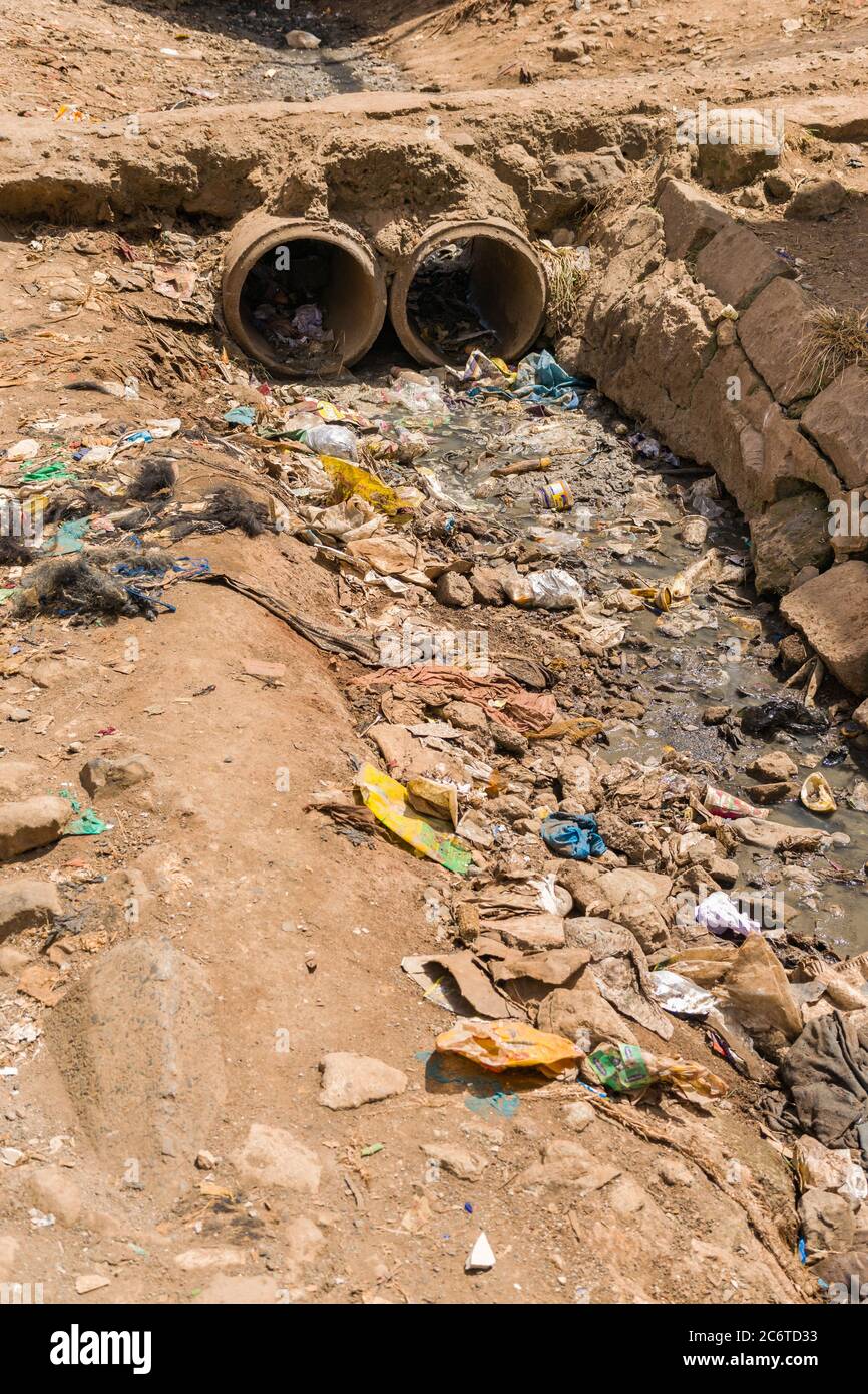 An open sewer filled with rubbish by the side of a dirt alley ...