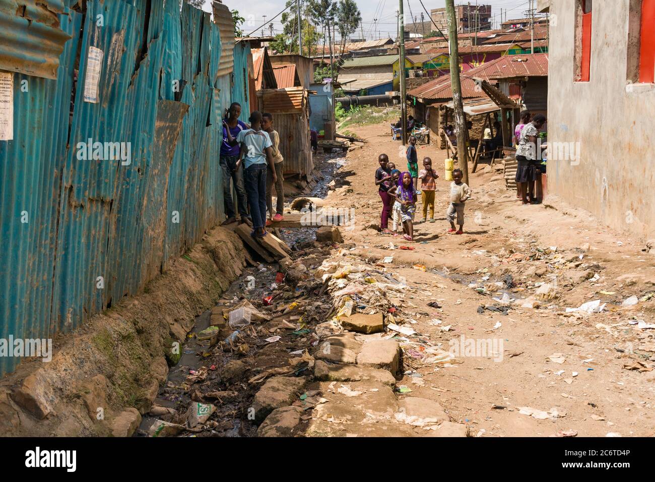 Children playing on a dirt alley way with open sewer filled with ...