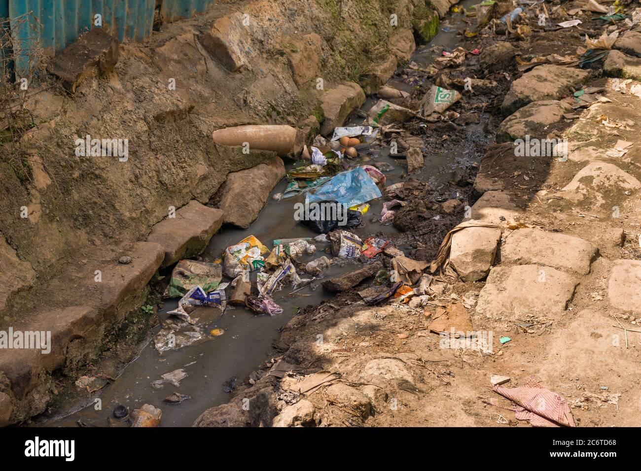 An open sewer filled with rubbish by the side of a dirt alley ...