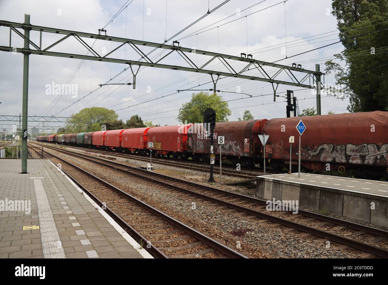 Freight locomotive with cargo wagons along platform of train station ...