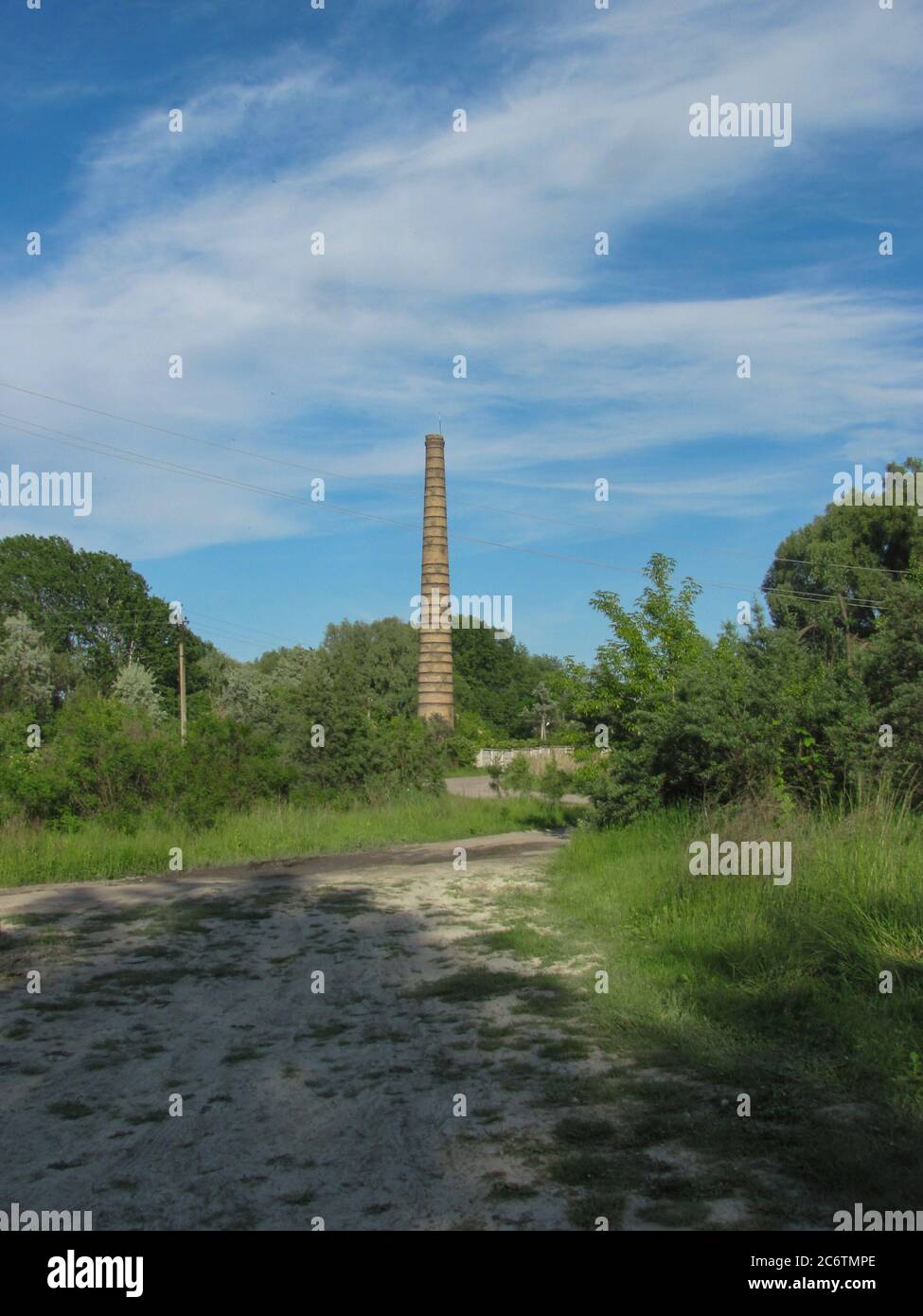 old chimney stack between green bushes under a blue sky - and a road ...