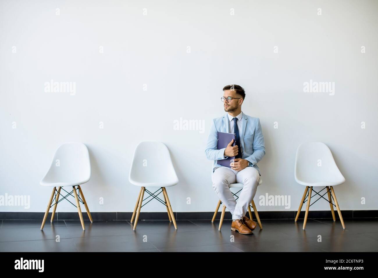 Young man sitting at chair in the waiting room with a folder in hand ...