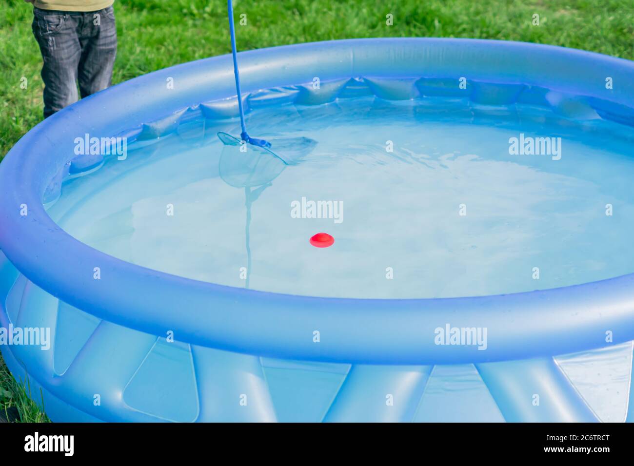 cleaning of garden swimming pool . Boy tries to cach red ball with ...