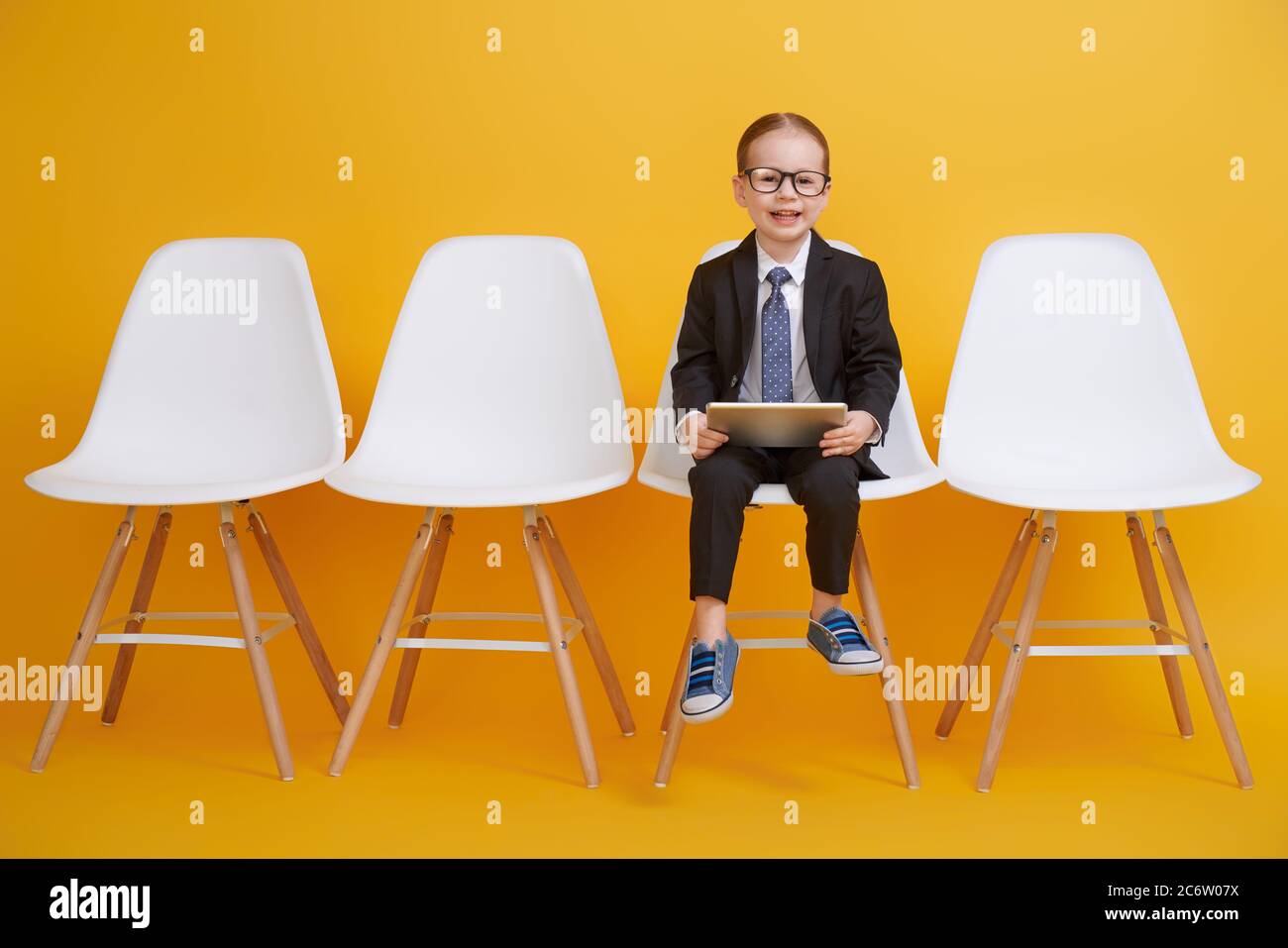 Cute baby girl working on a tablet on bright yellow wall background ...