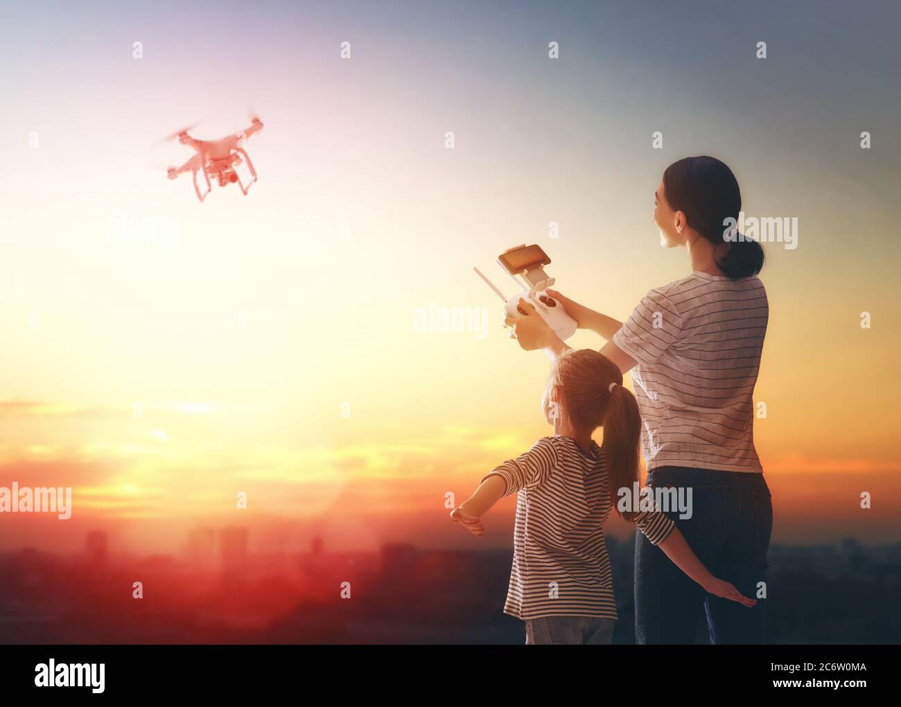 Little girl and her mother are operating the drone by remote control in ...