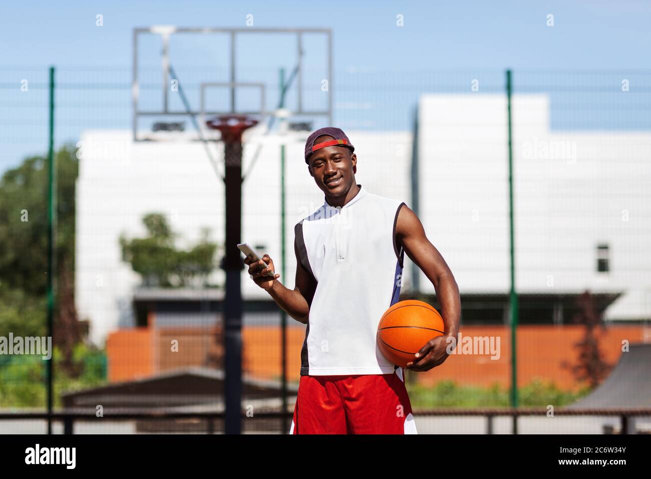 Happy black basketballer with mobile phone standing at outdoor game ...