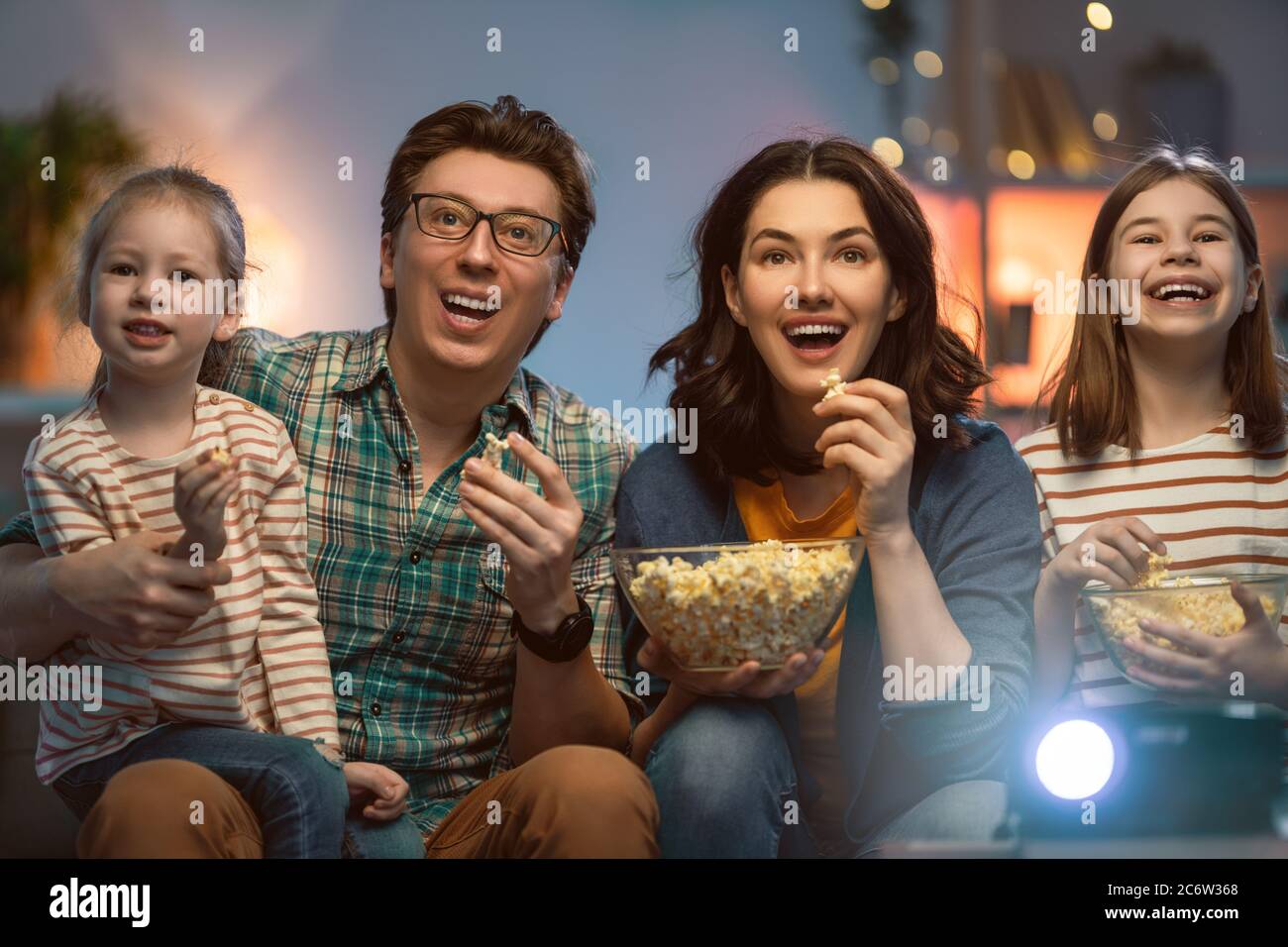 Happy family watching projector, TV, movies with popcorn in the evening ...