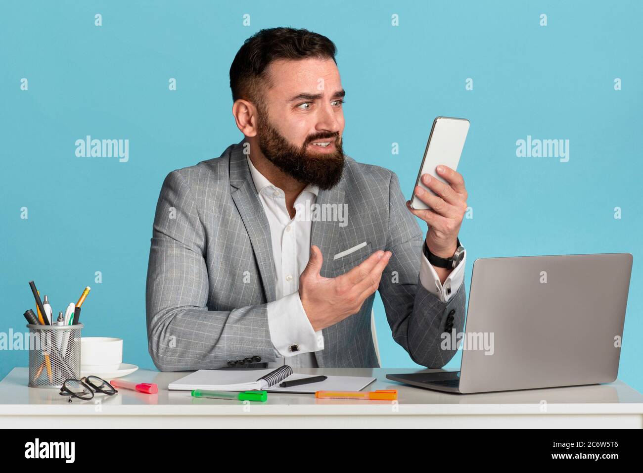 Annoyed office employee with smartphone and laptop computer sitting at ...