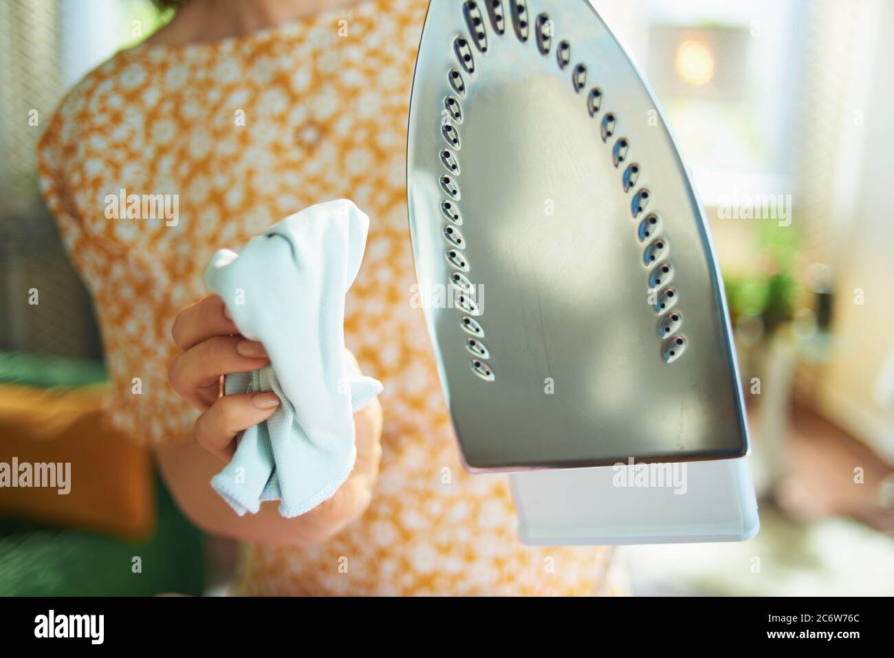 Closeup on woman in yellow dress cleaning iron with cloth in the living ...