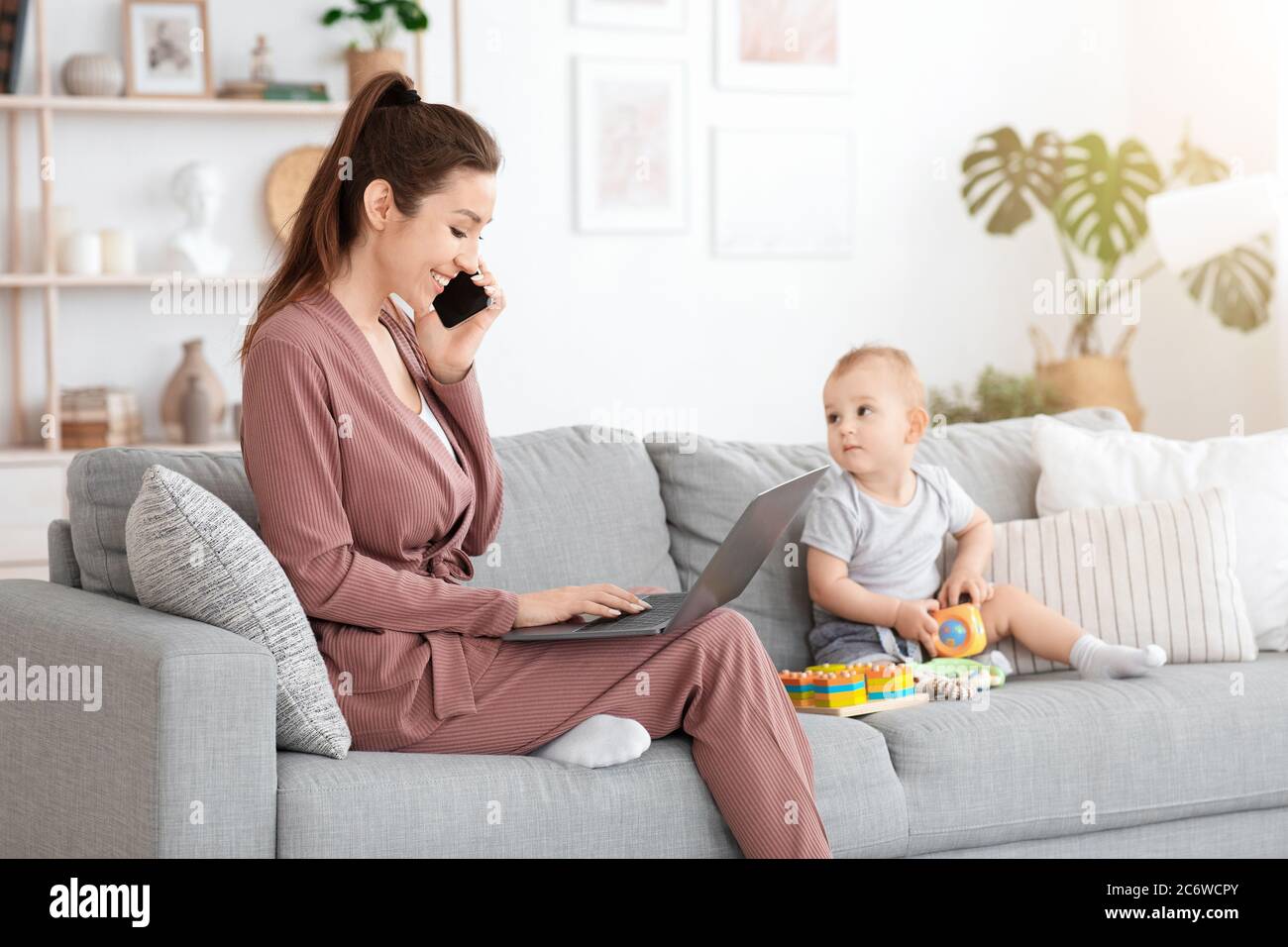 Busy Mom Working With Laptop And Cellphone While Taking Care Of Baby ...