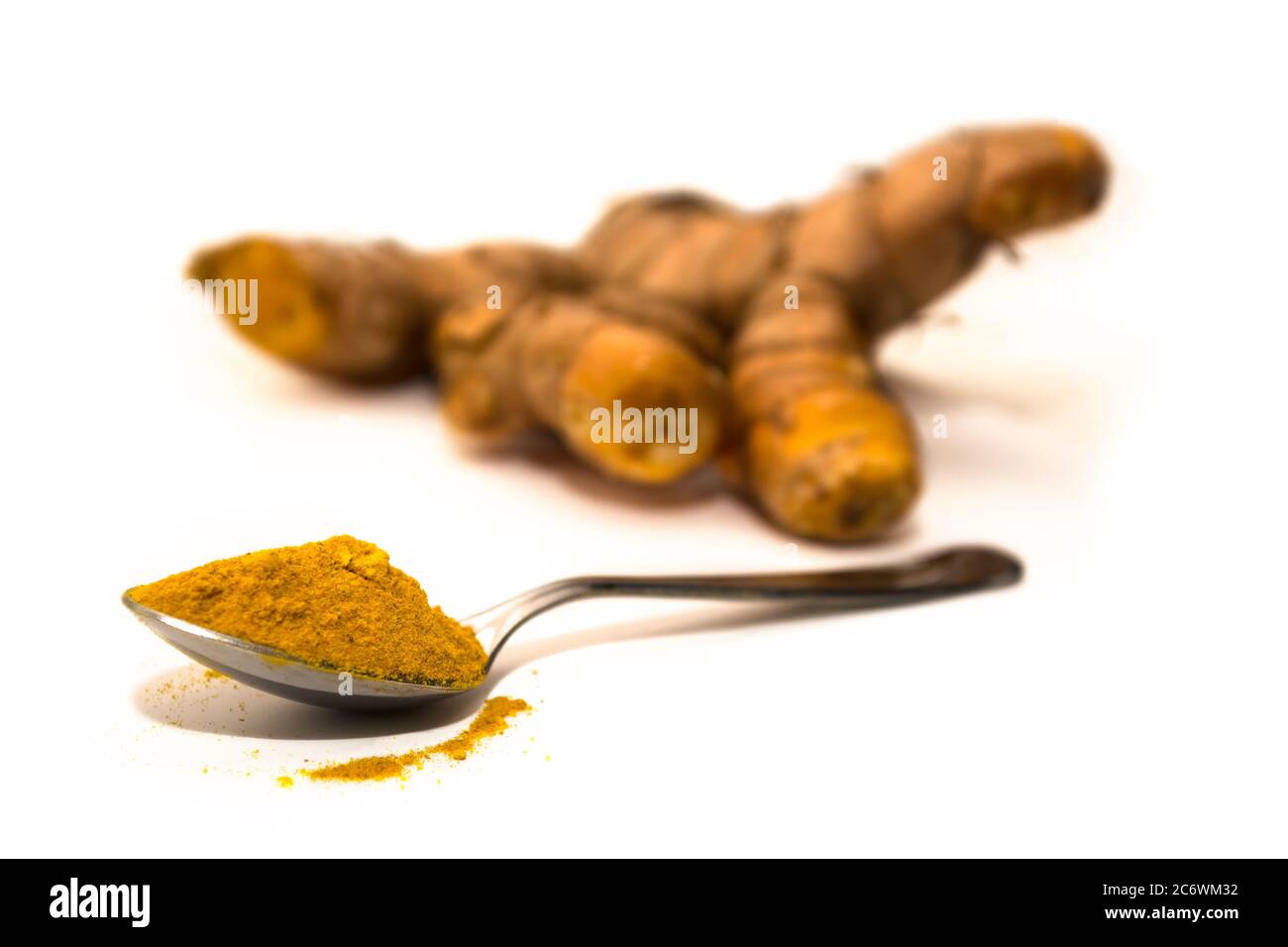 Fresh turmeric root and a spoon with dried turmeric powder on a white ...