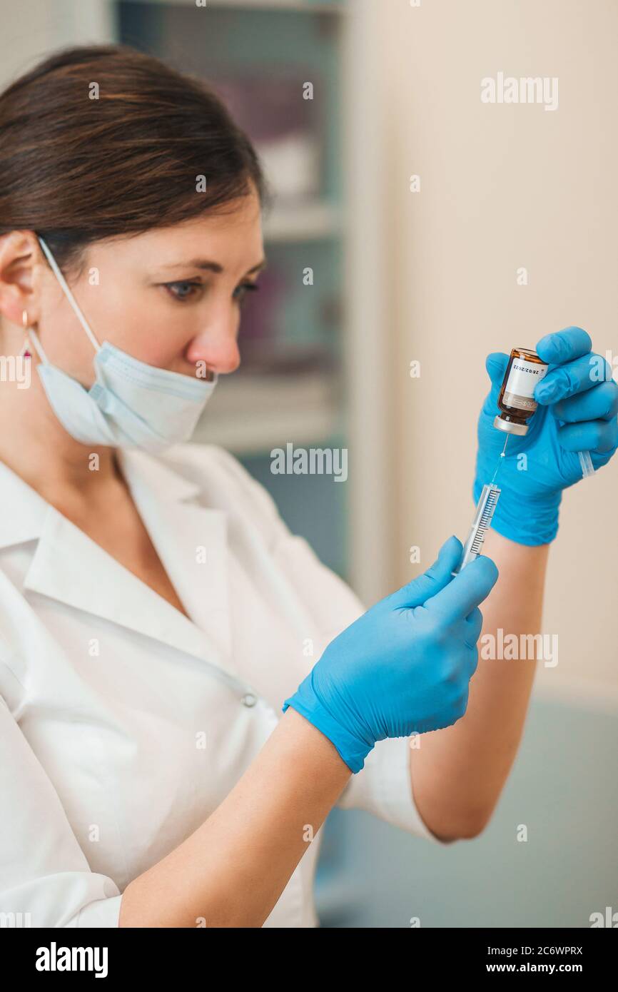 Female doctor draws a solution into a syringe from an ampoule ...