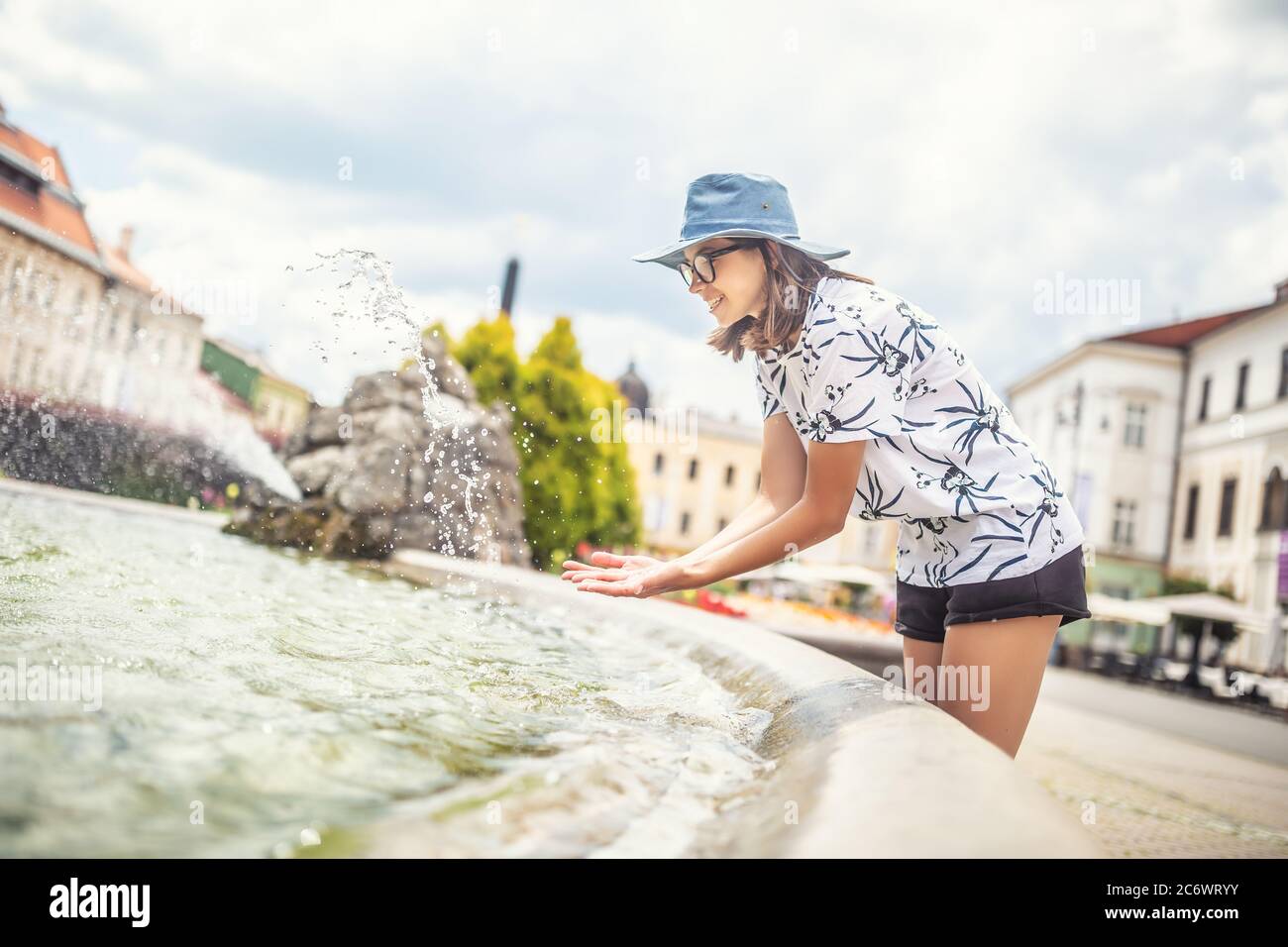 Teenage girl refreshing in a fountain on a hot summer day in the city ...