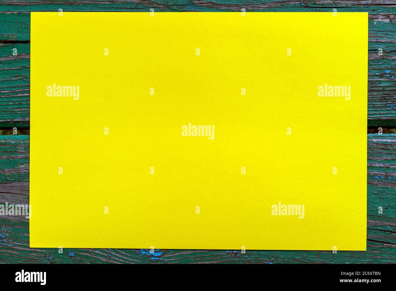 Blank yellow paper on green wooden surface. Template, wallpaper, poster ...