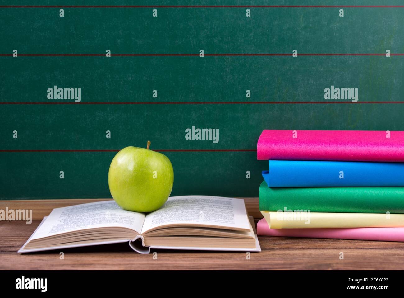 Apple and coloured books on the chalkboard background, back to school ...