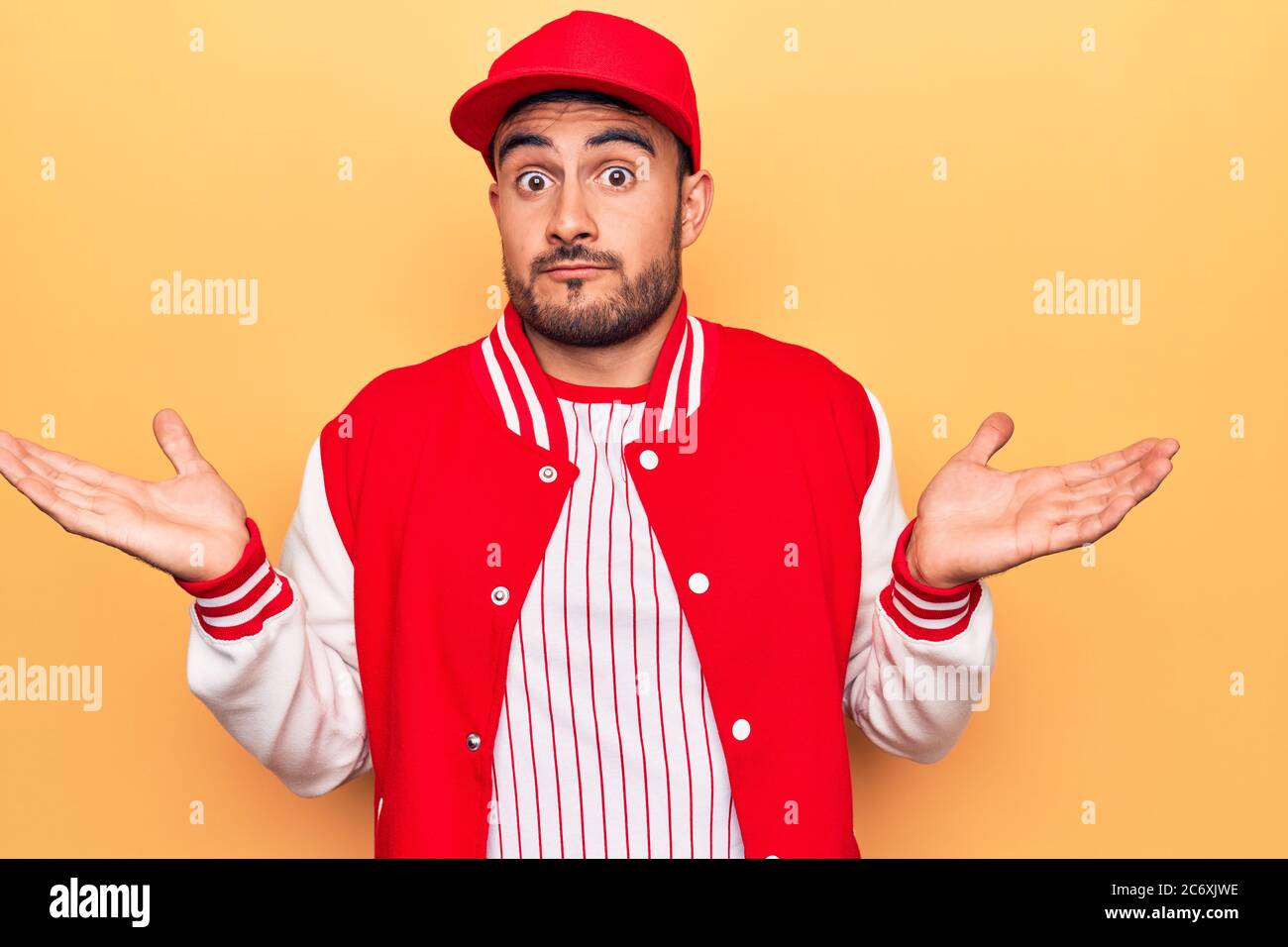 Handsome sporty man with beard wearing baseball jacket and cap over ...