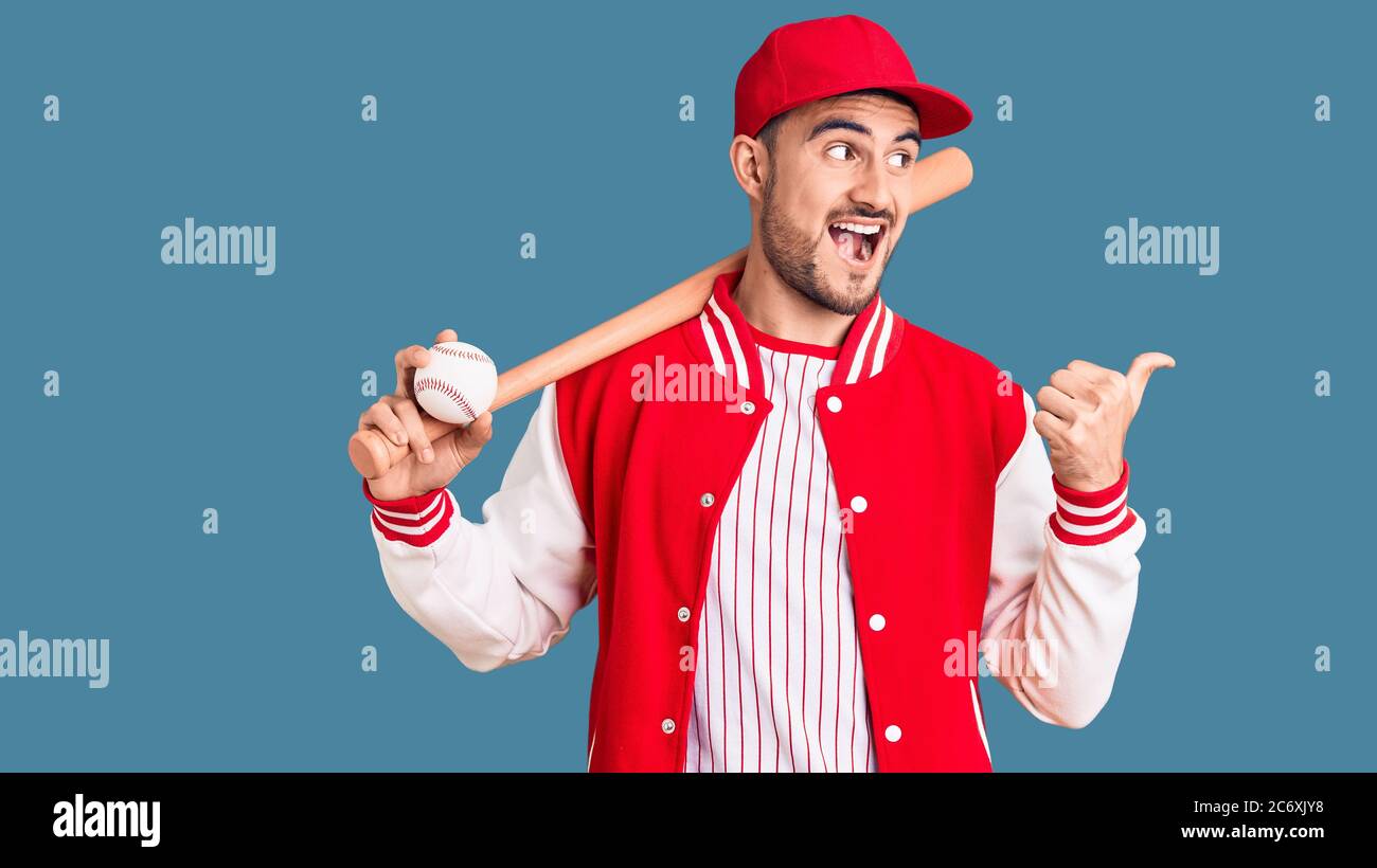 Young handsome man holding baseball bat and ball pointing thumb up to ...