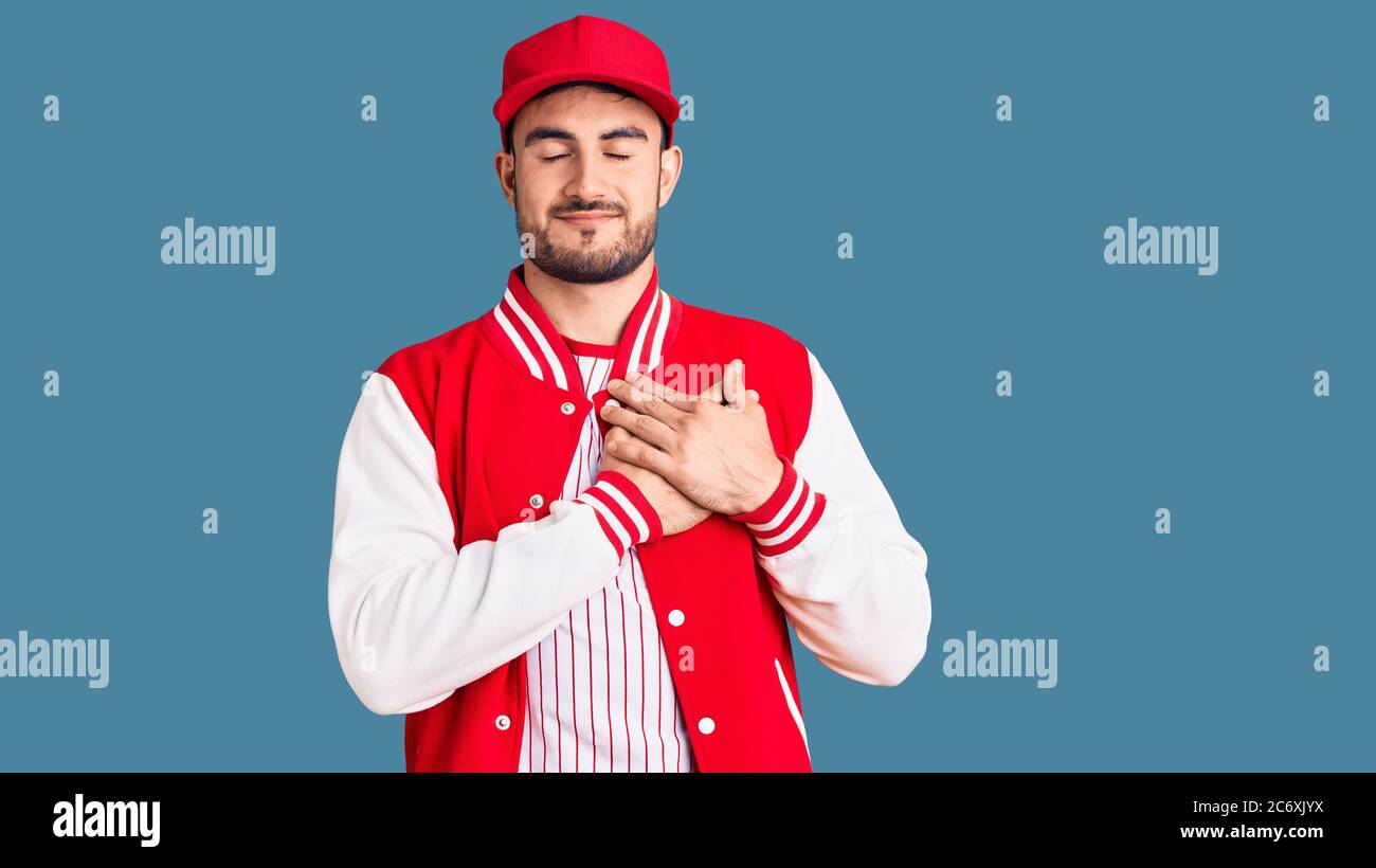 Young handsome man wearing baseball jacket and cap smiling with hands ...