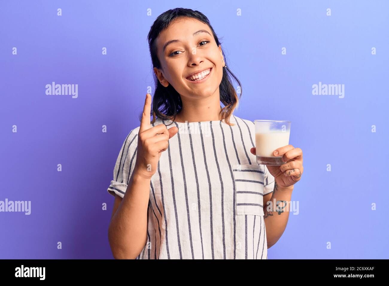 Young woman holding glass of milk smiling with an idea or question ...