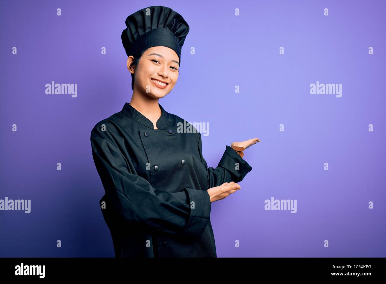 Young beautiful chinese chef woman wearing cooker uniform and hat over ...