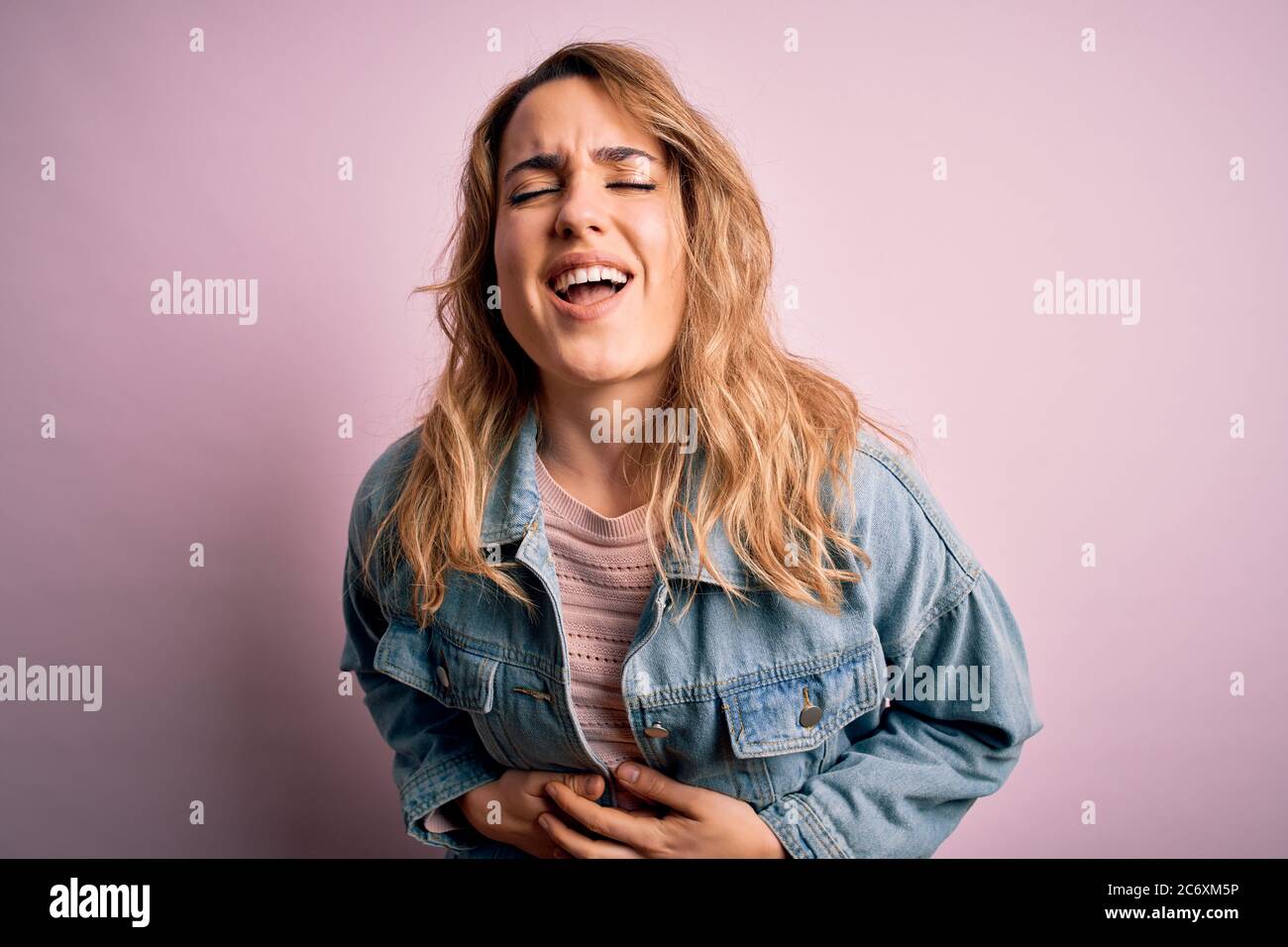 Young beautiful blonde woman wearing casual denim jacket standing over ...