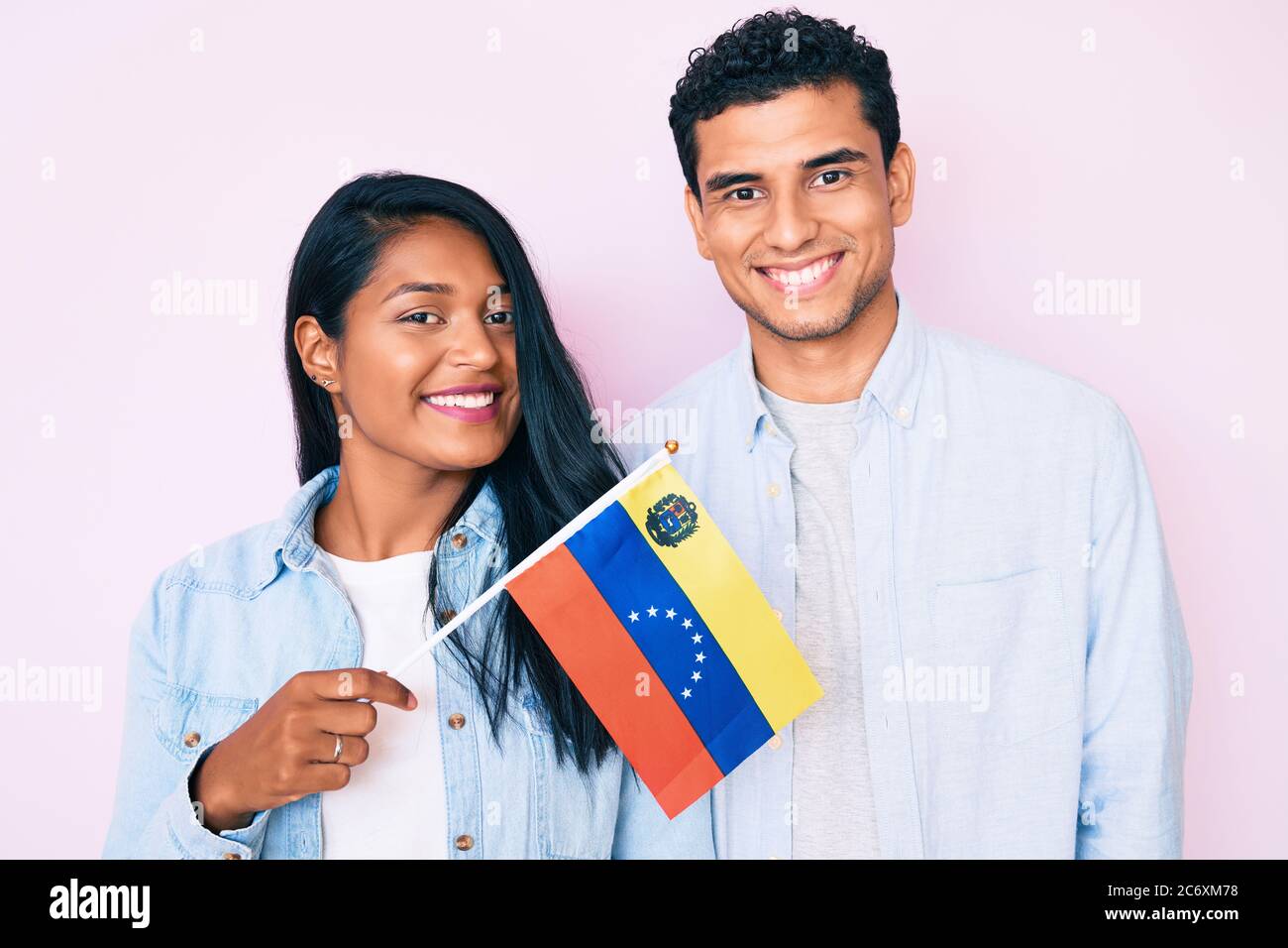 Beautiful latin young couple holding venezuelan flag looking positive ...